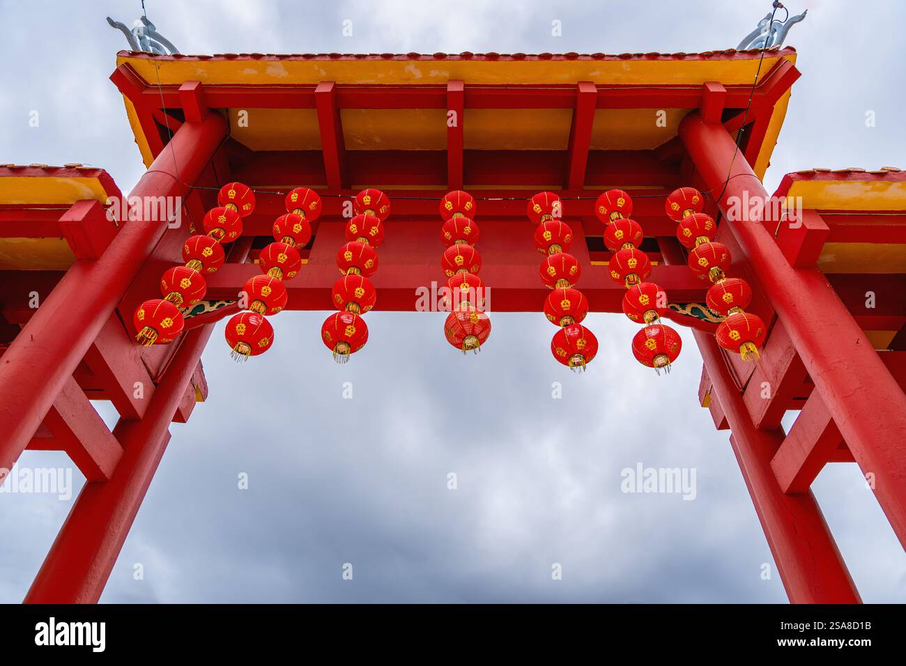 A red temple archway with hanging red lanterns against a cloudy sky at ...
