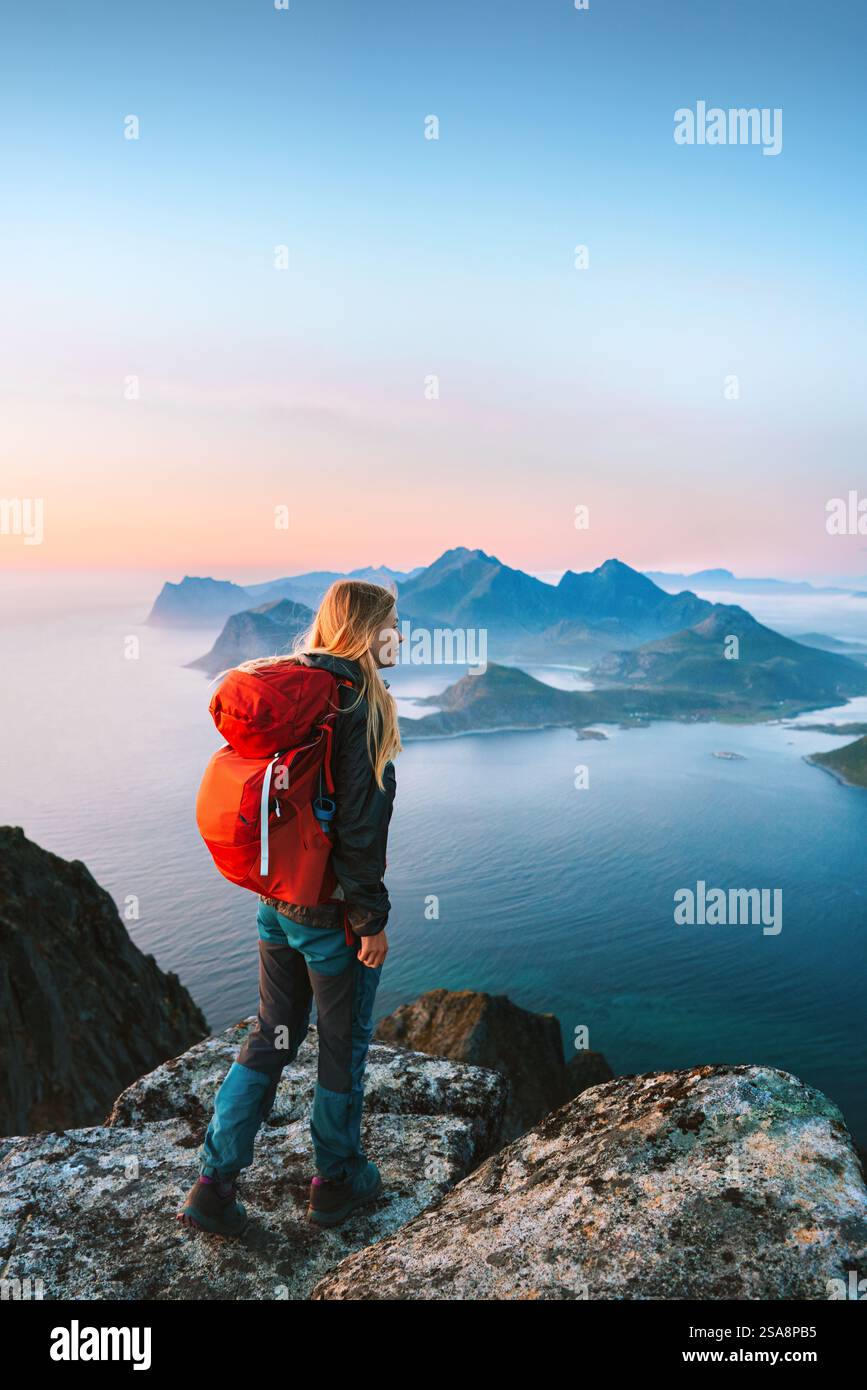 Woman with red backpack hiking in Norway girl traveler on mountain cliff edge in Lofoten islands ...