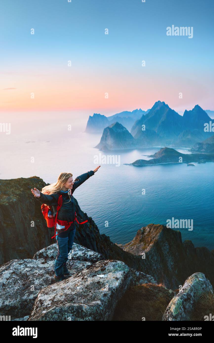 Woman traveling in Lofoten islands solo traveler on mountain cliff edge enjoying sunset view ...