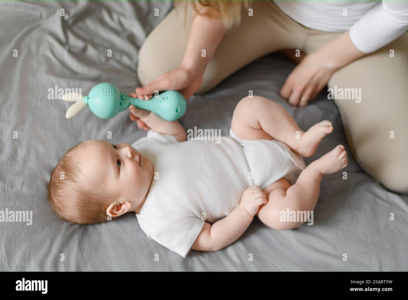 Cute baby is lying on bed, babbling. Mom gives baby a rattle in his ...