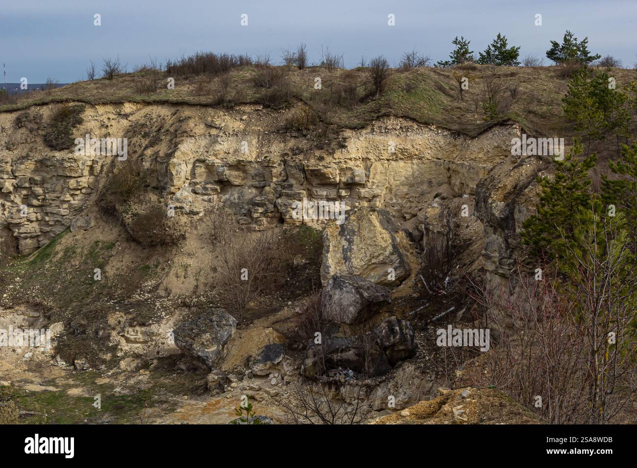 A rocky hillside features steep cliffs and patches of dry vegetation. The overcast sky adds a ...