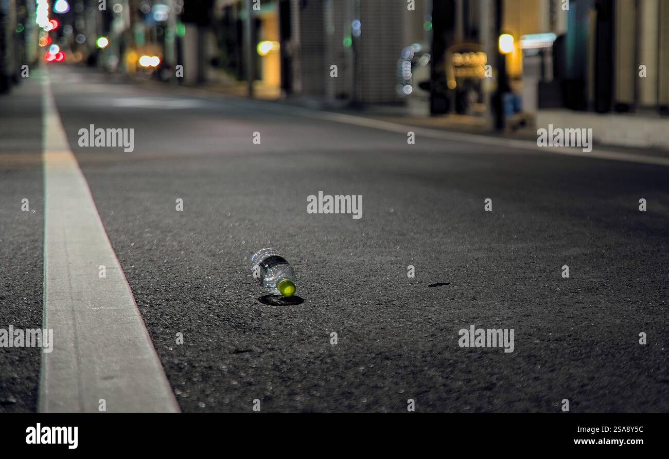 A single discarded plastic bottle lying on an empty street at night in ...