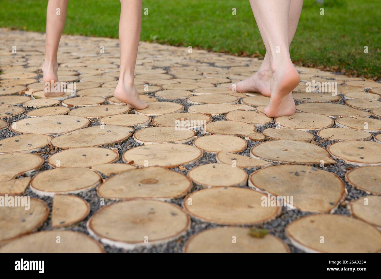 Two people walking barefoot on wooden path made of logs, enjoying ...