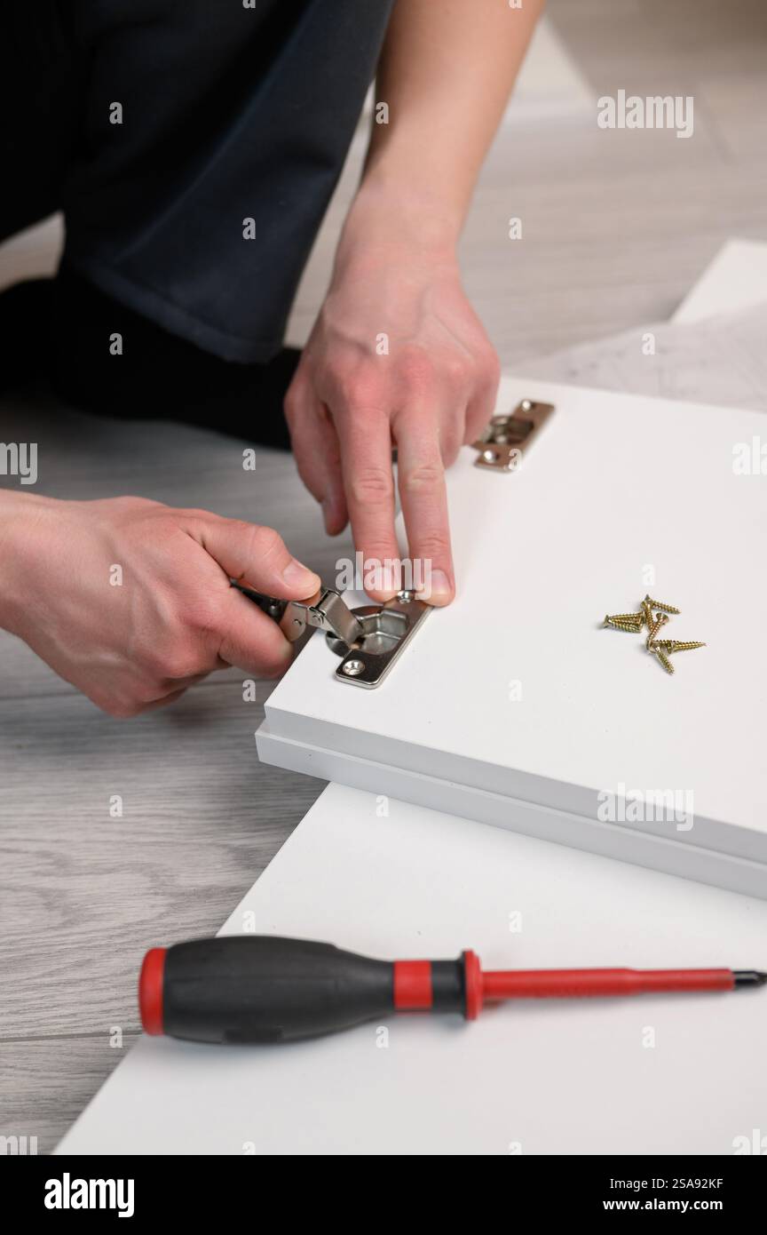 Assembling furniture. A worker inserts a hinge into a wooden closet ...
