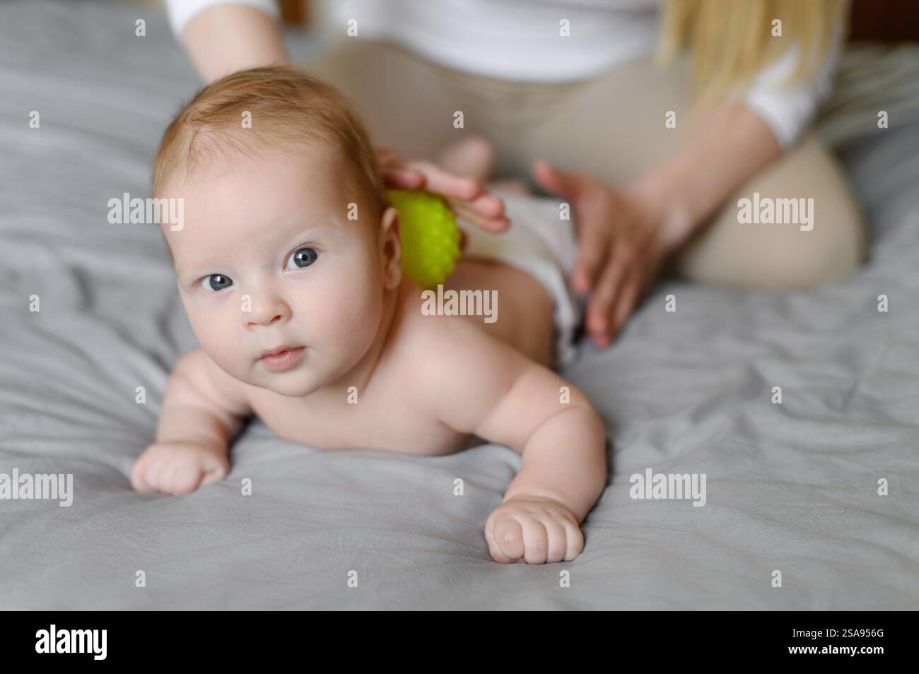 Mom massages the back of the baby with a massage ball. The baby lies on ...