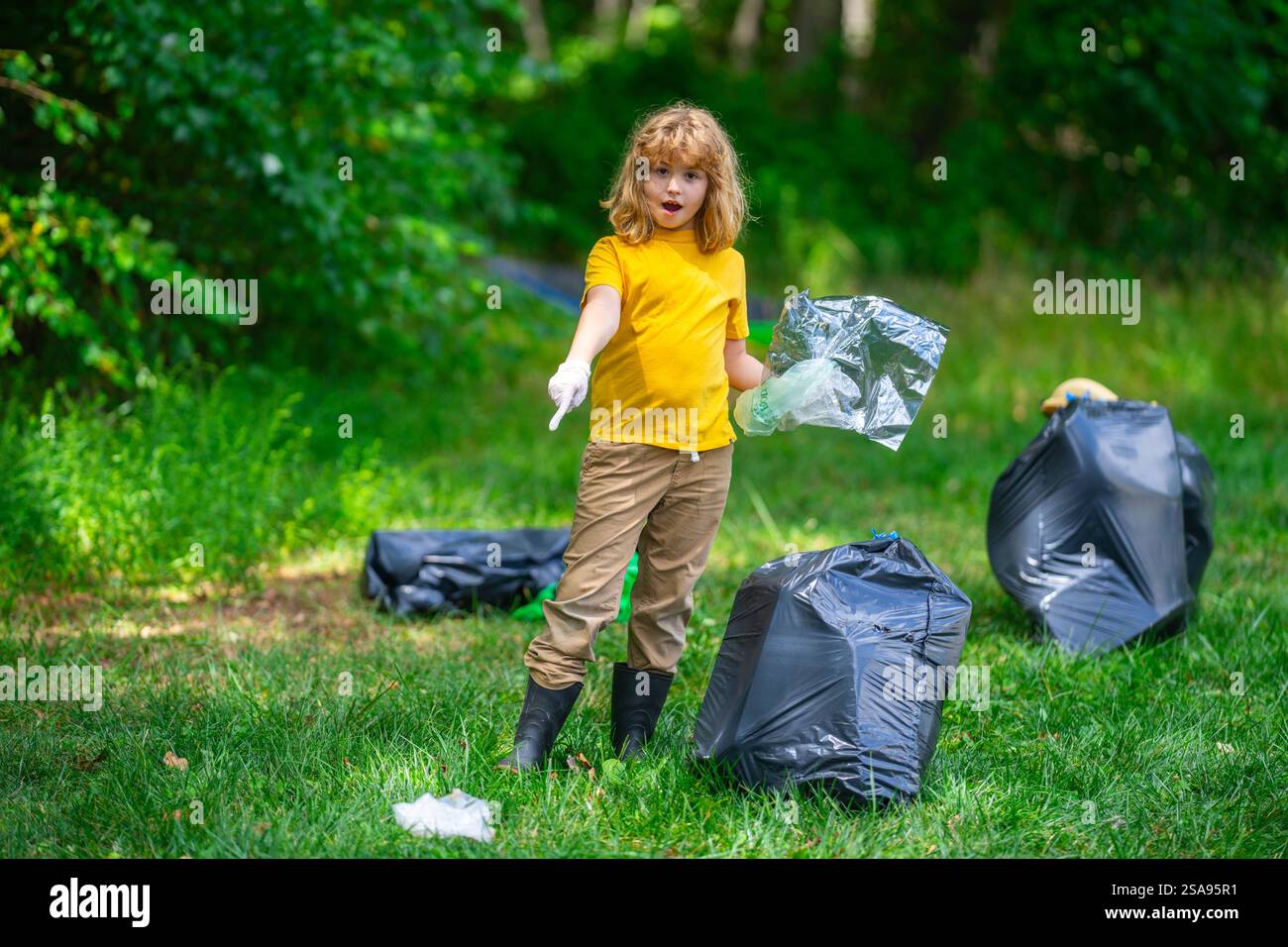 Kid in rubber gloves with trash bag clean up garbage on forest outdoor ...