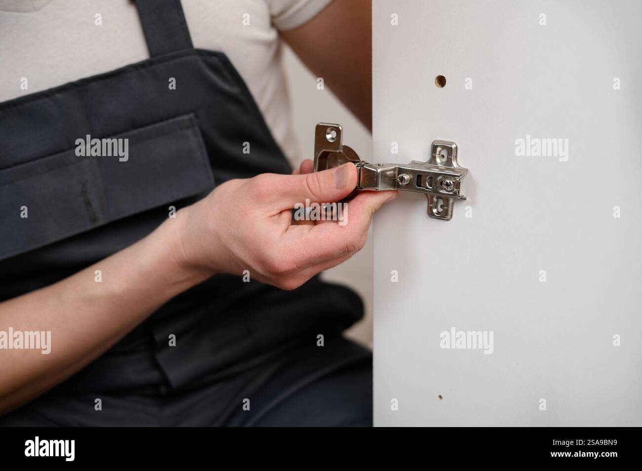Assembling furniture. A worker inserts a hinge into a wooden closet ...