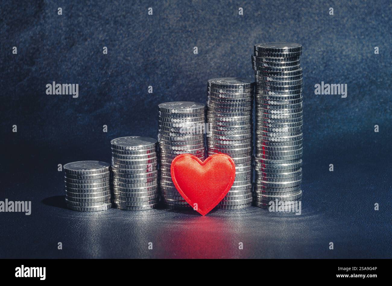 One red heart on columns of shiny coins. Dark blue background ...