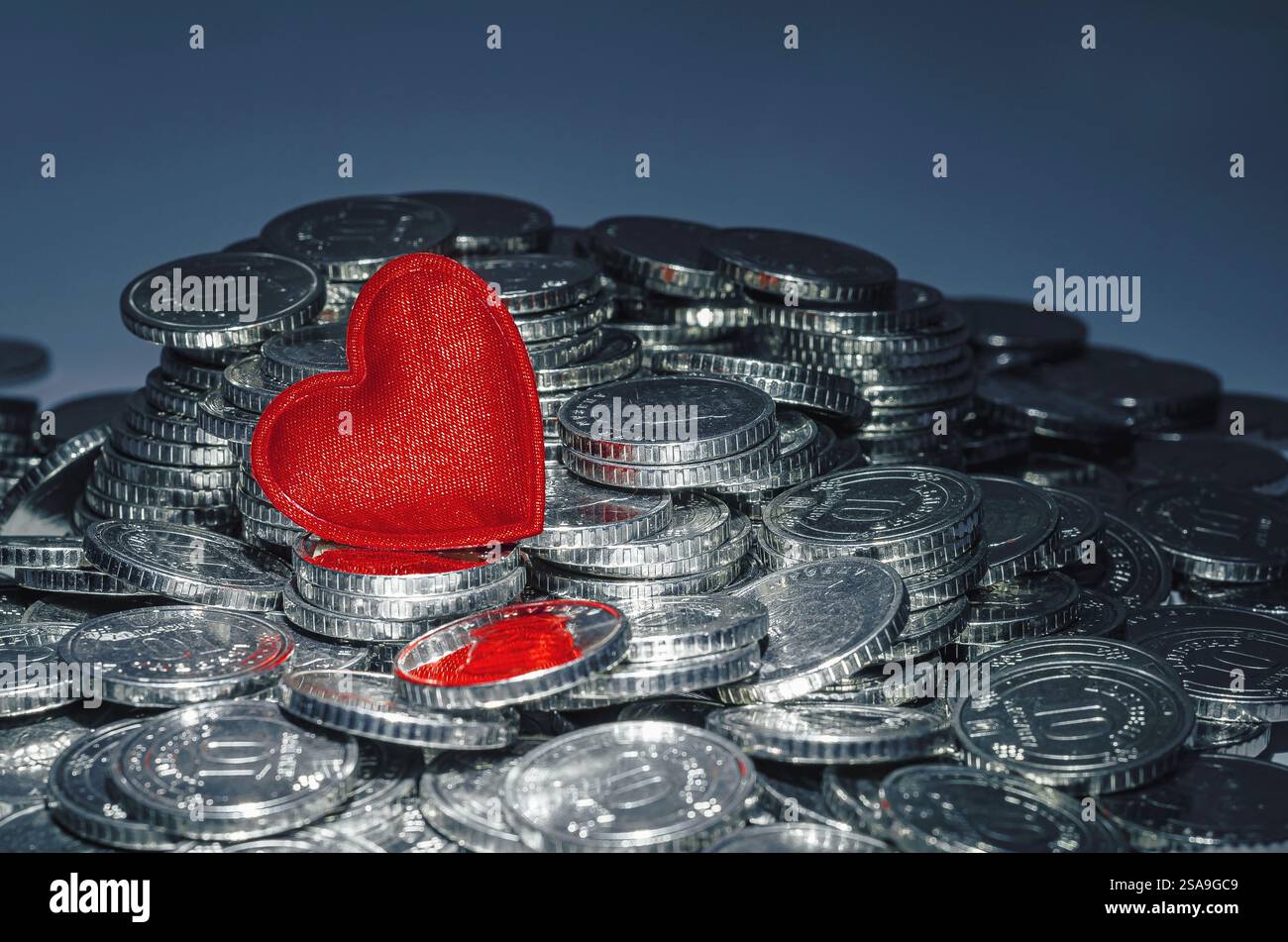 Red heart on pile of shiny coins. Dark blue background. Valentine's Day ...