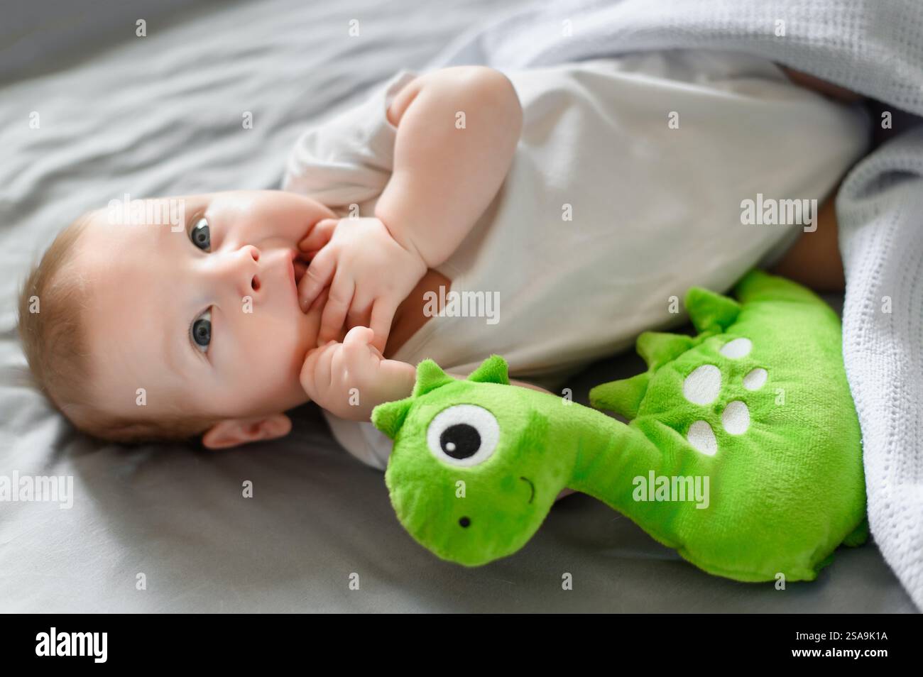 Cute baby lies under blanket in his crib and holds his fingers in his ...