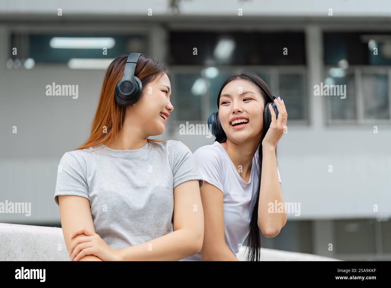 Two happy students sharing music through headphones in an outdoor ...