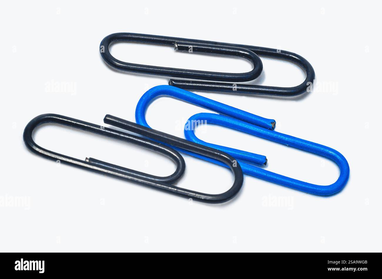 Two black and one blue paper clips lie on white background, isolated ...