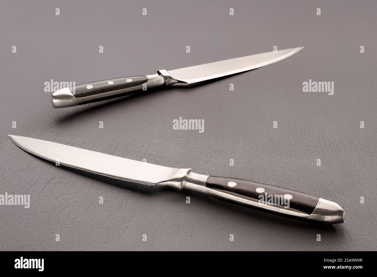 Two metal knives on a slate stone, close-up, isolated on a white ...