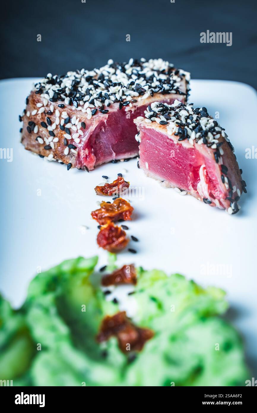 Tuna slices with green puree, sesame seeds and sun-dried tomatoes on a ...