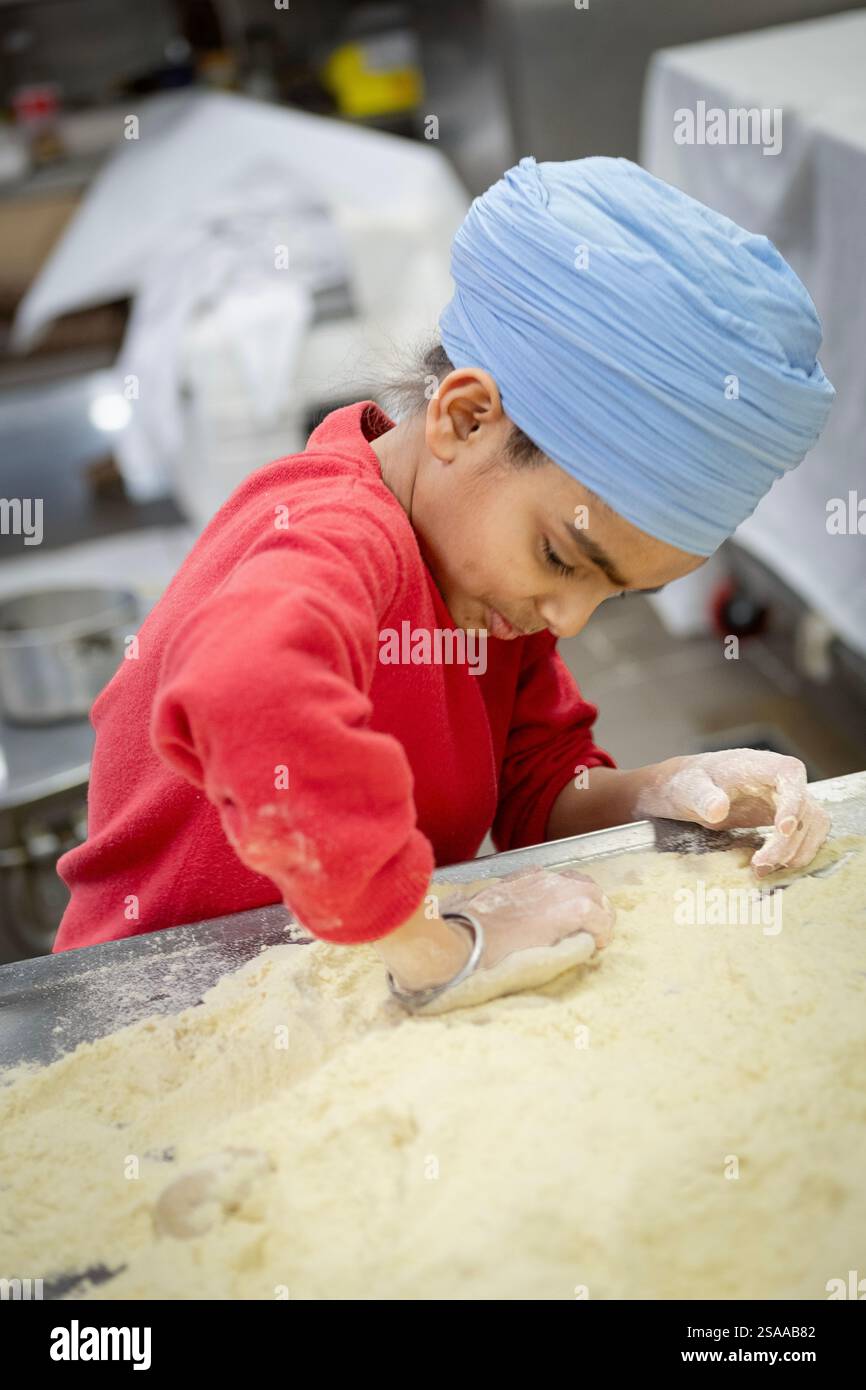 A young Sikh boy in a blue turban helps make roti bread for the temple ...