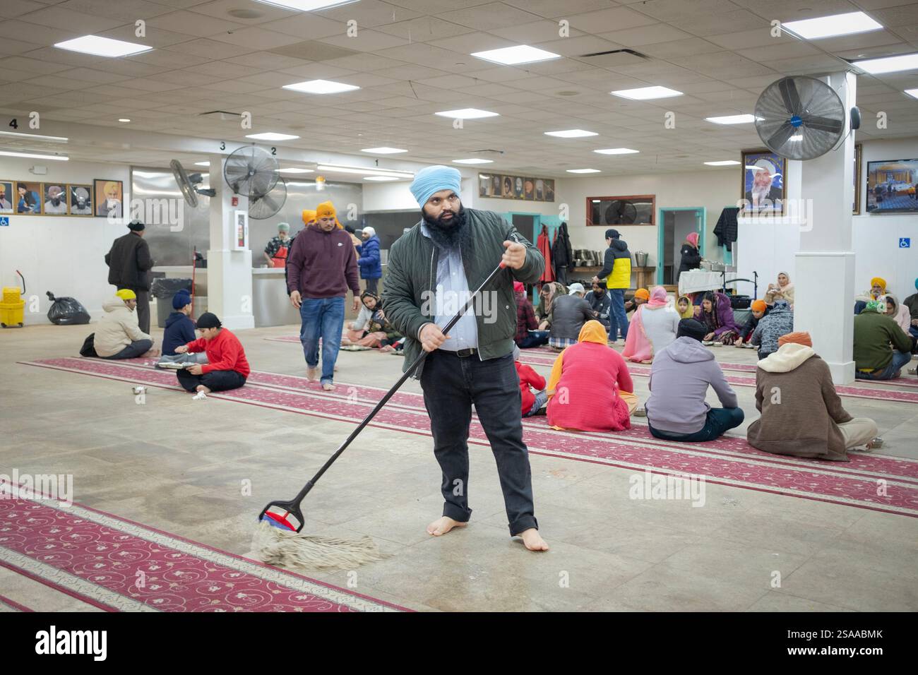 A volunteer in a blue turban mops the floor in a langar communal ...