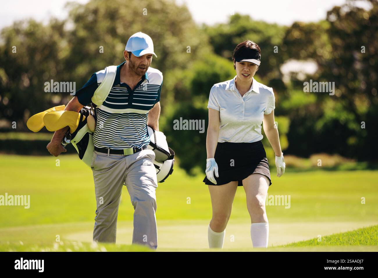 Sportswoman and caddy walking on a golf course, carrying a golf bag and ...