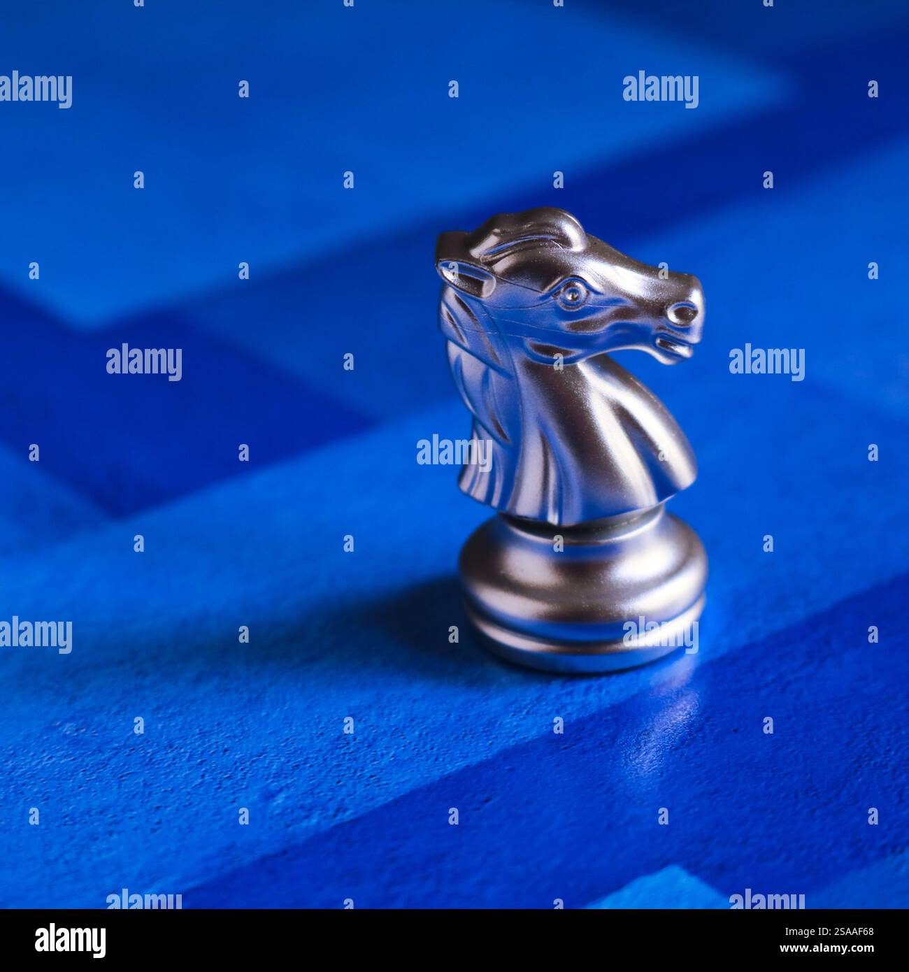 Distinct silver chess knight piece positioned on a blue chessboard with ...