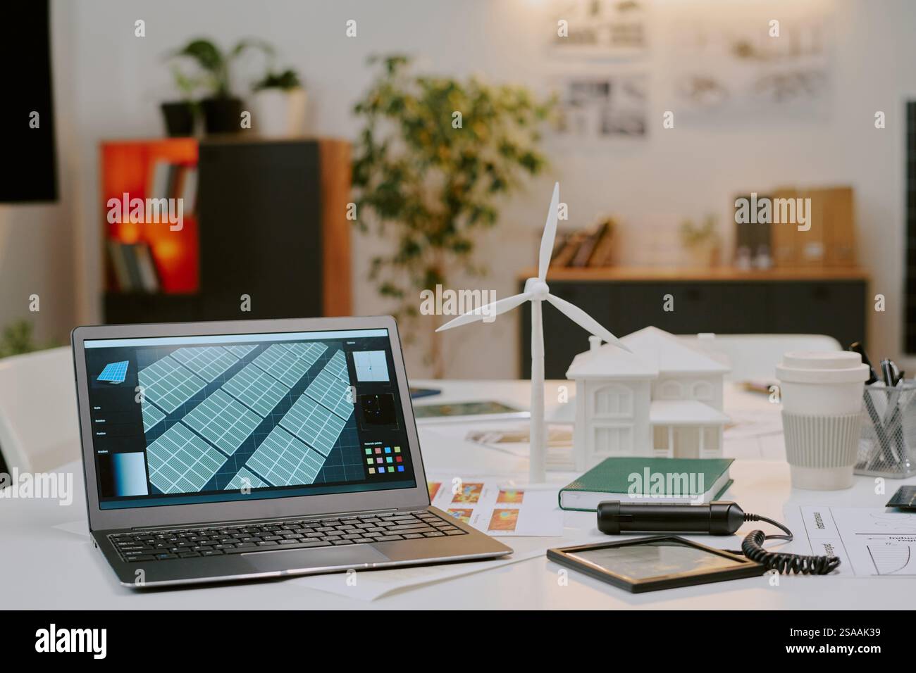Workspace setting featuring laptop displaying solar panel design and miniature wind turbine ...