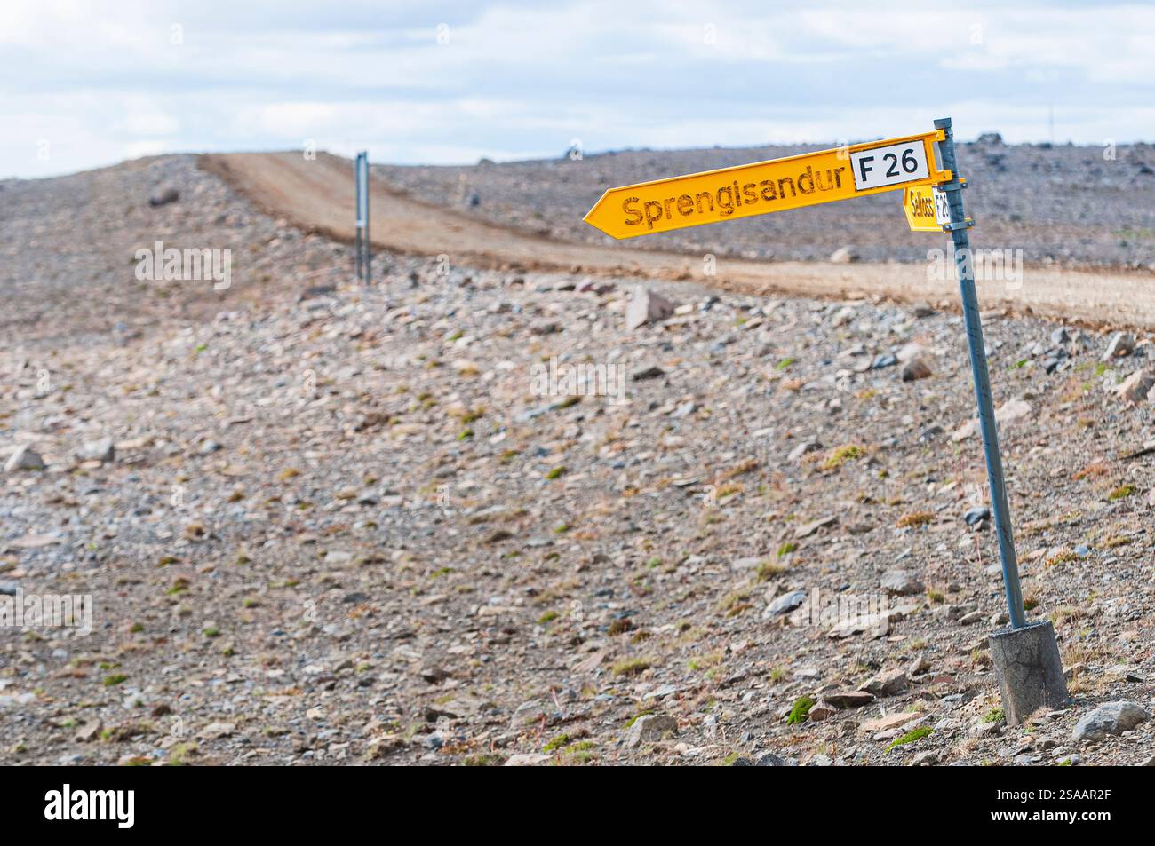 A gravel road stretches into the distance, marked by a bright yellow ...