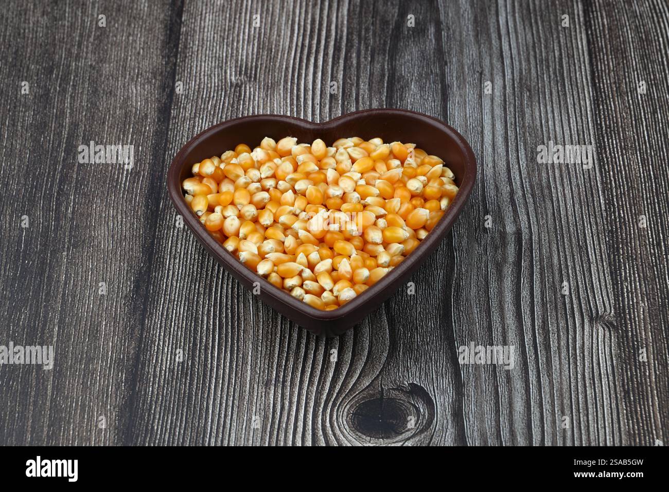 Unpopped popcorn in a wooden bowl on wooden background. A type of corn ...