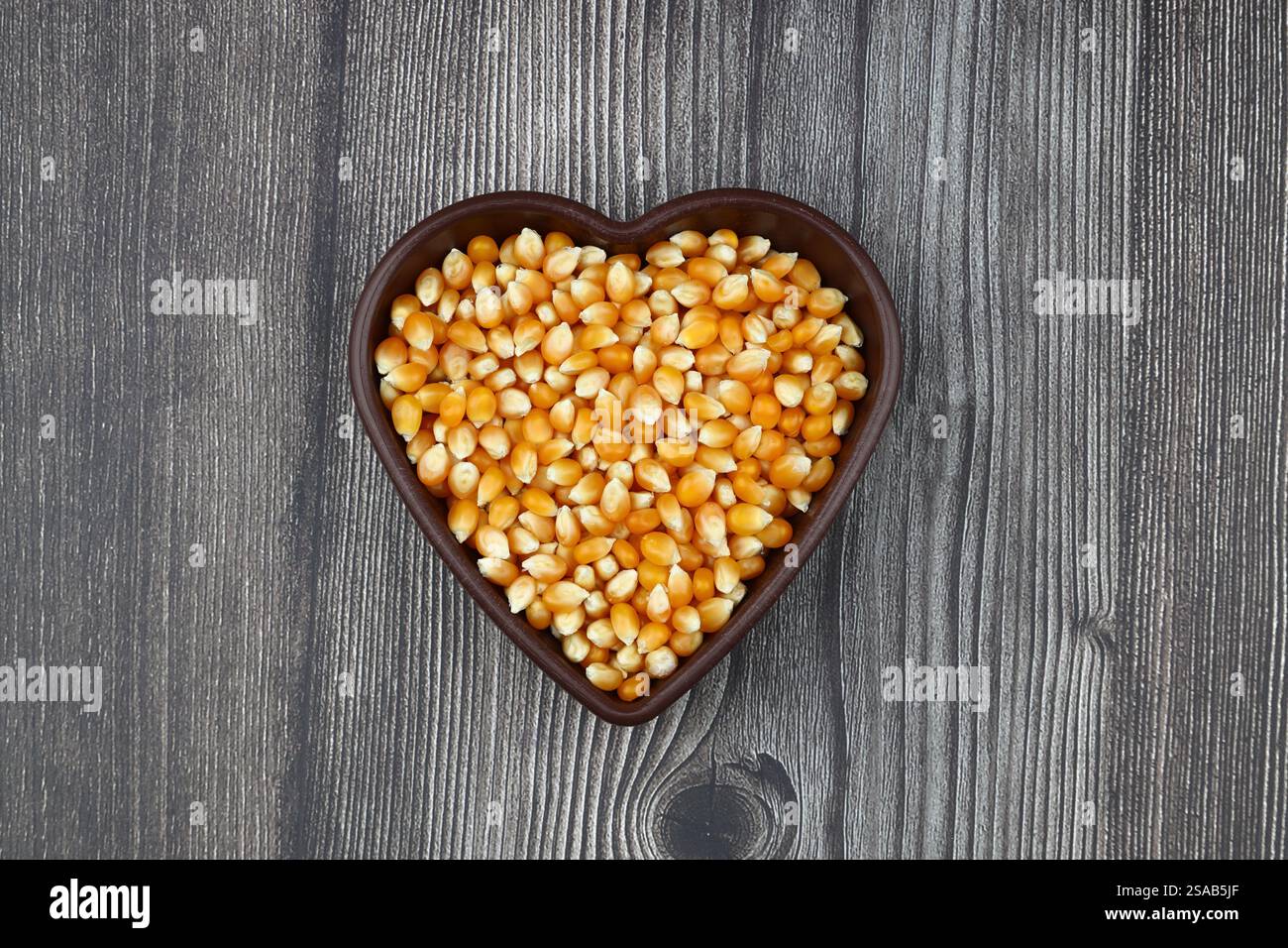 Unpopped popcorn in a wooden bowl on wooden background. A type of corn ...
