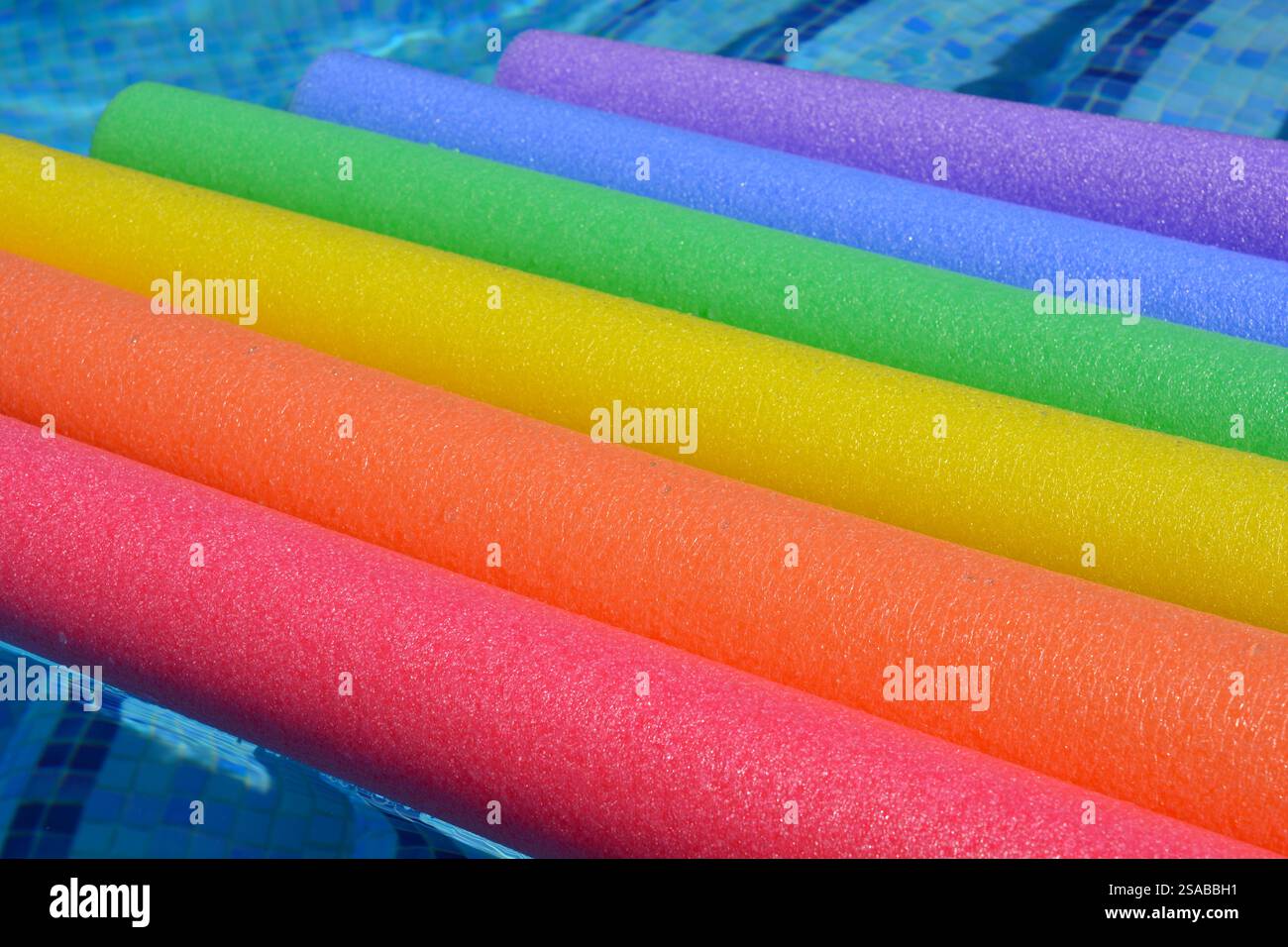 Rainbow coloured swimming pool noodles floating on water, bright and ...