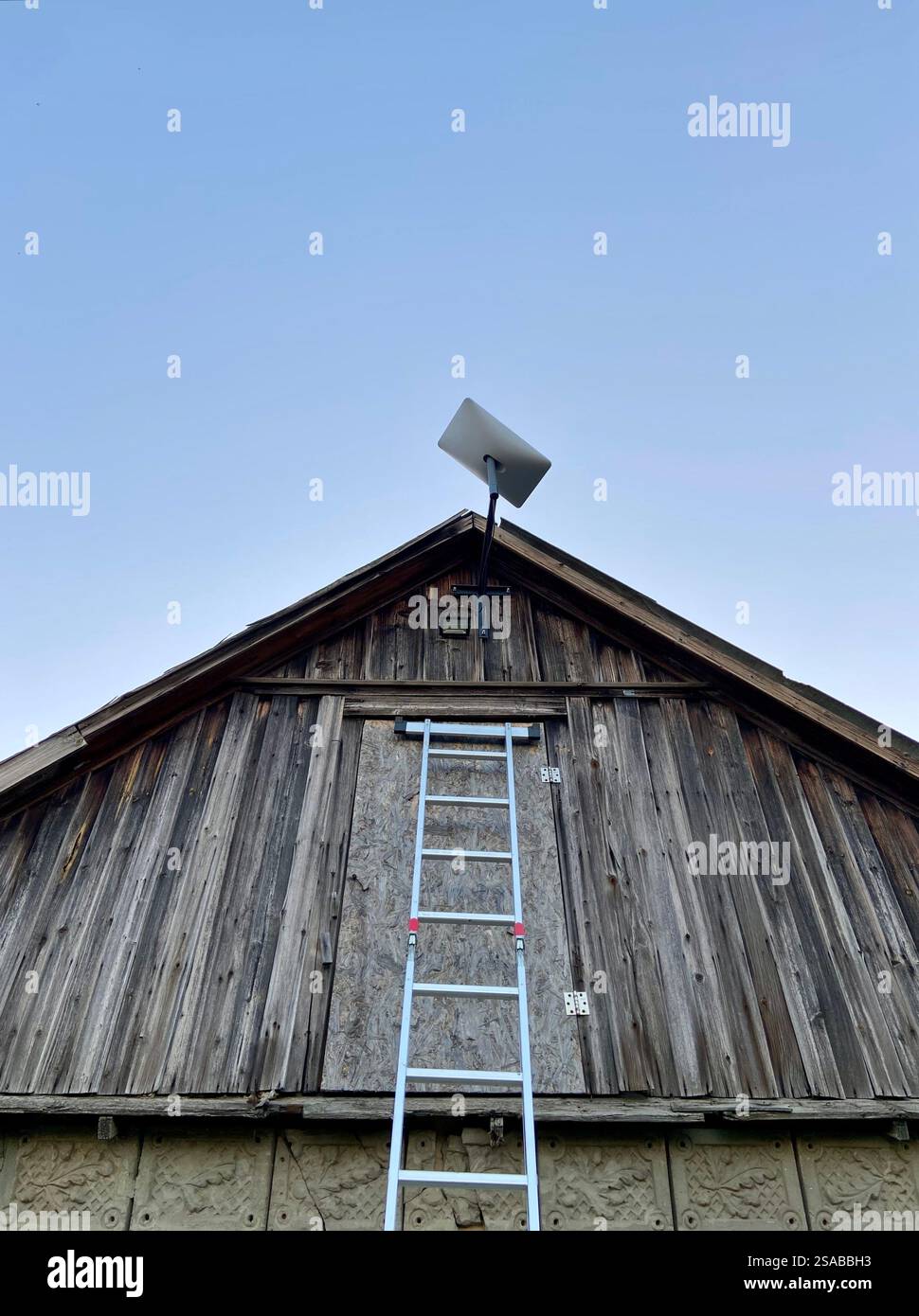 A modern square satellite dish mounted on the roof of a rustic wooden ...