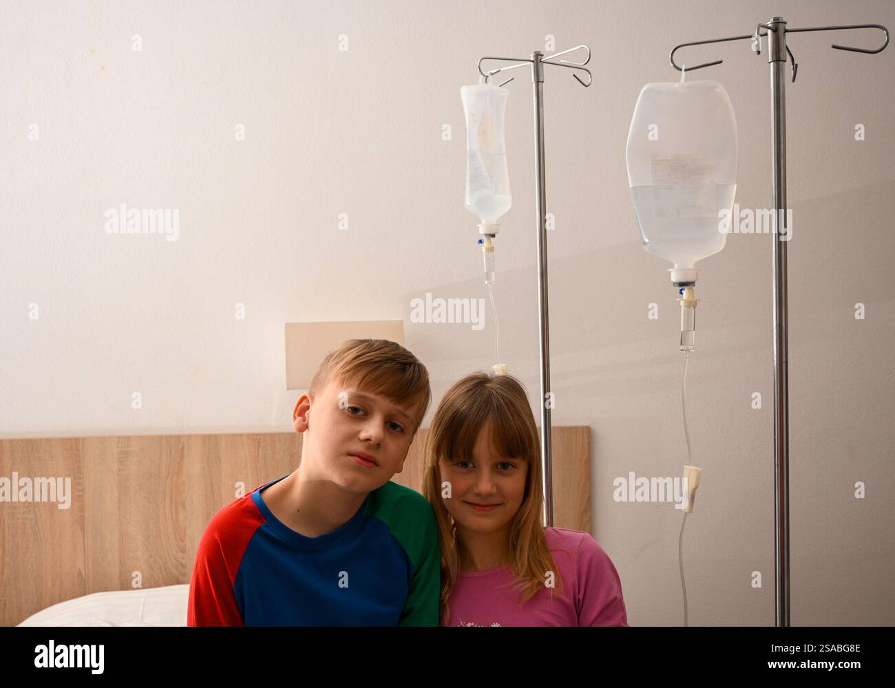 Brother and sister patients sitting on bed with intravenous drips in ...