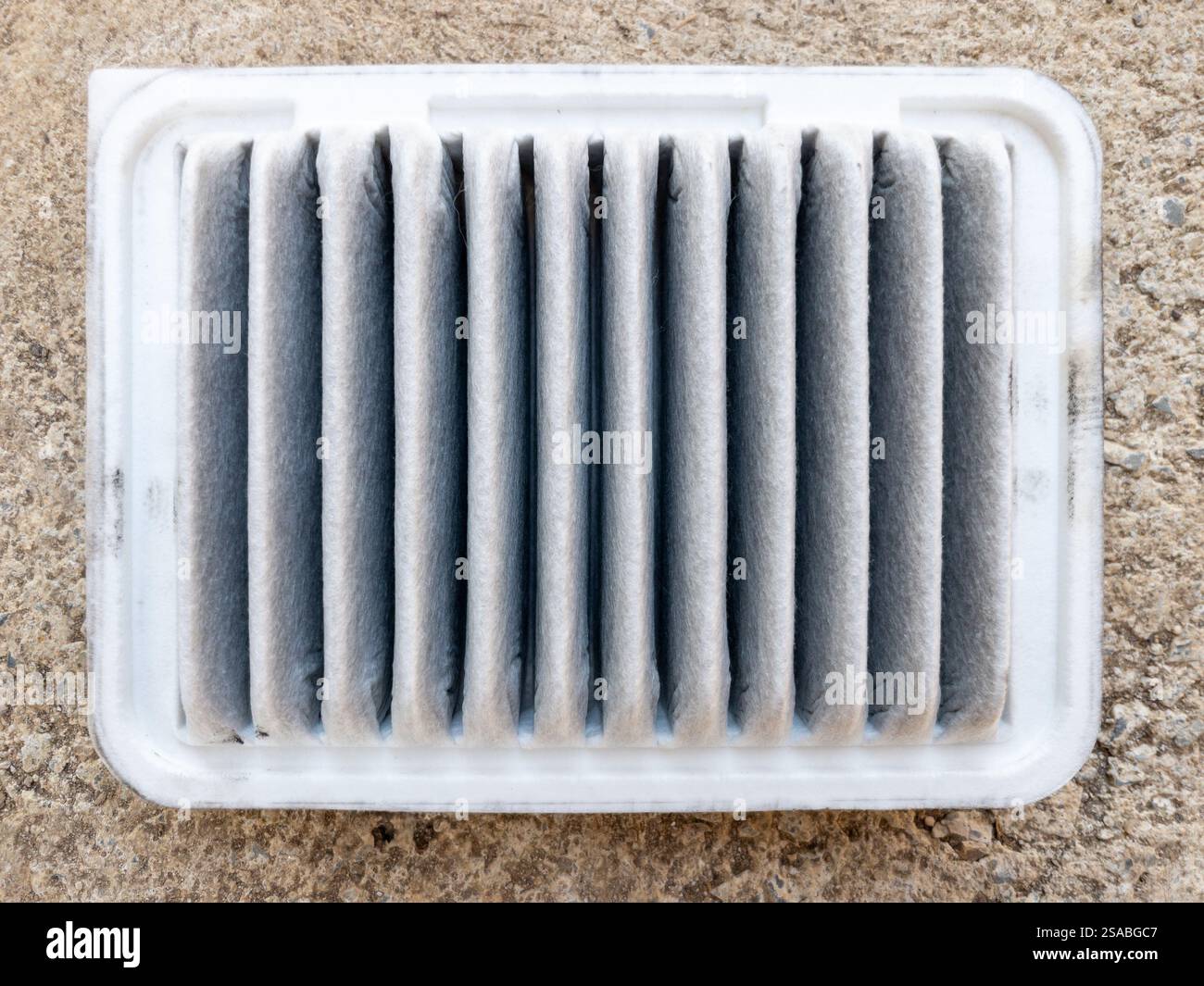 A close-up of a used car air filter covered in accumulated dirt and ...