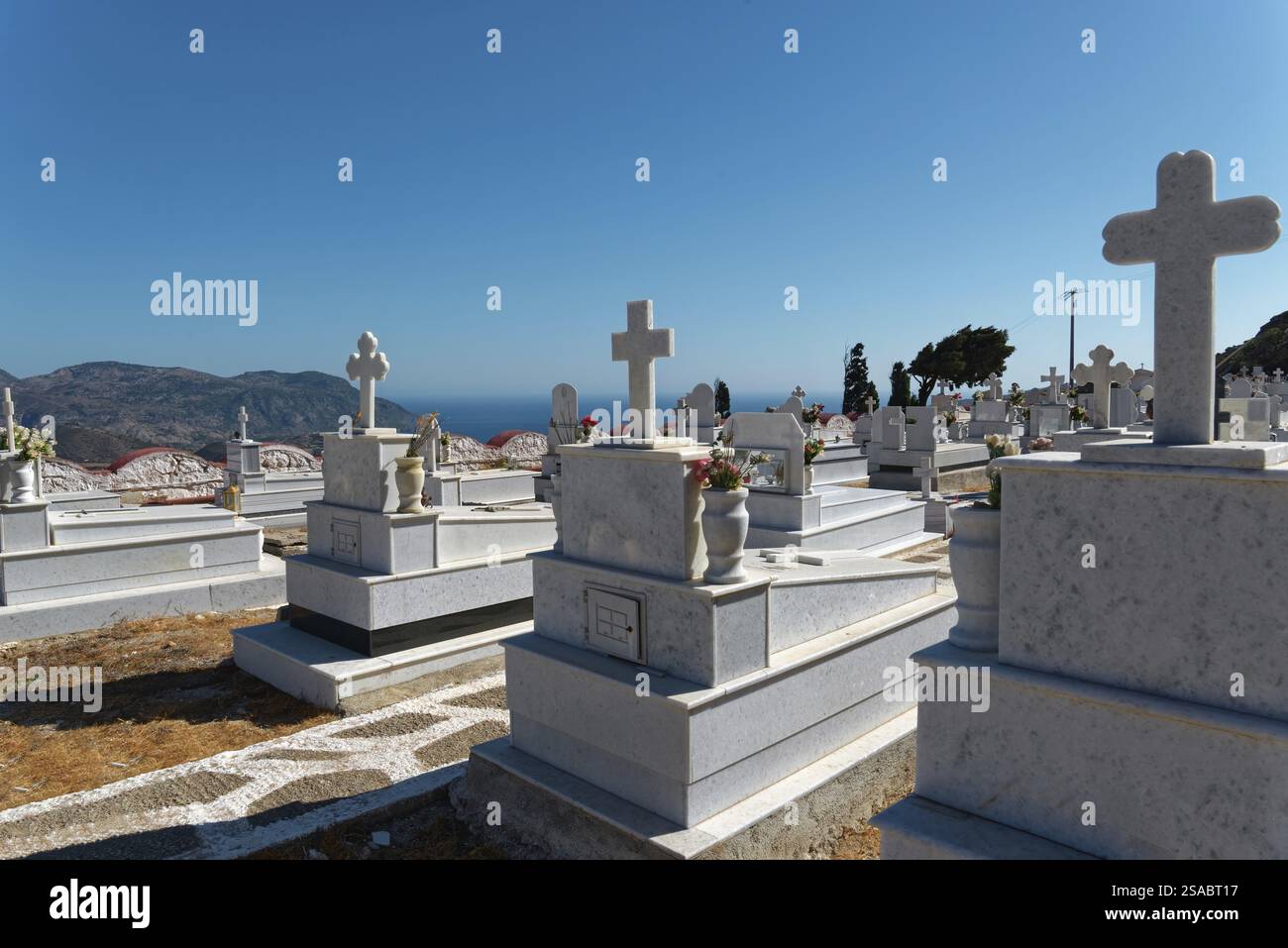 White cemetery of Menetes with stone grave crosses and sea view under a ...