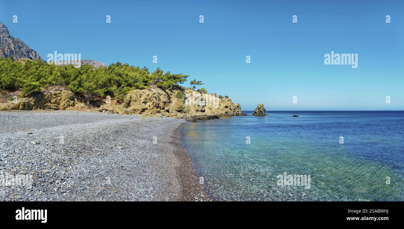 Quiet pebble beach with clear blue water and green pine trees, hiking ...