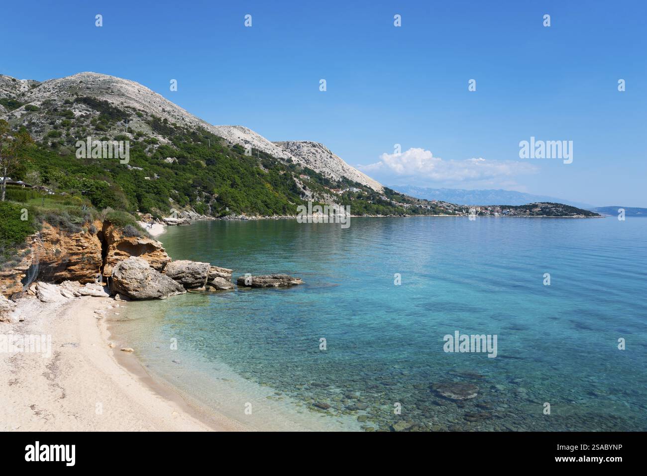 Clear blue sea water on a sandy beach with rocky coastline under a ...