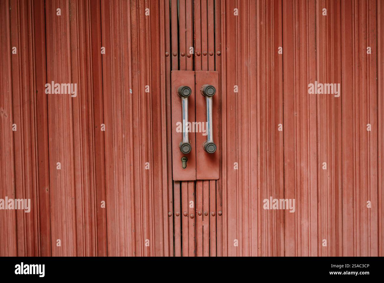 Close-up of a weathered red rolling shutter door with metal handles ...