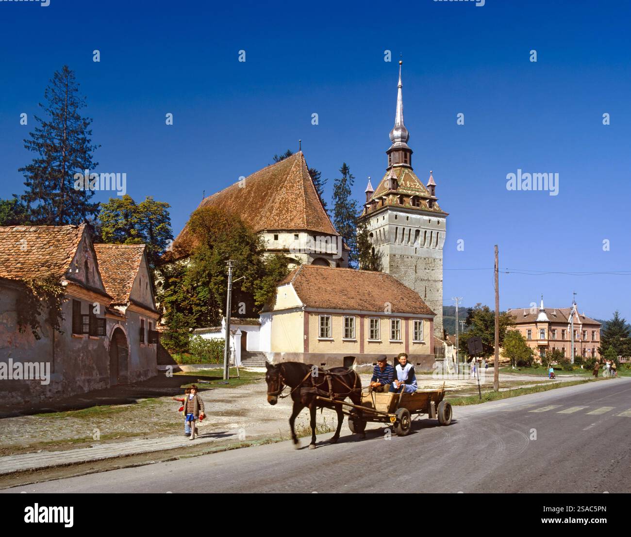 Traditional horse-drawn wagon passing church at Saschiz, Transylvania ...