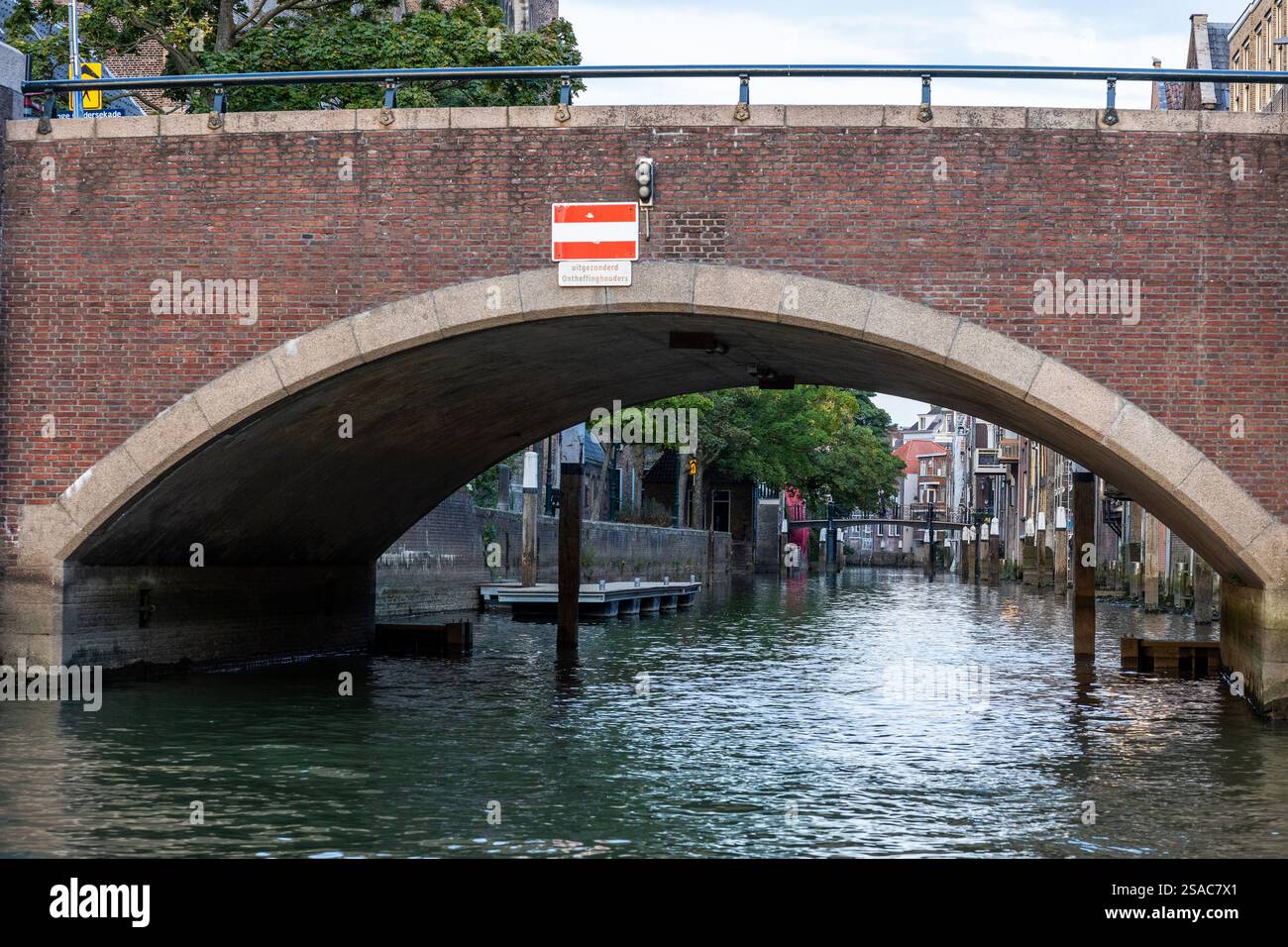 A brick arch bridge spans a calm canal, reflecting historic buildings ...