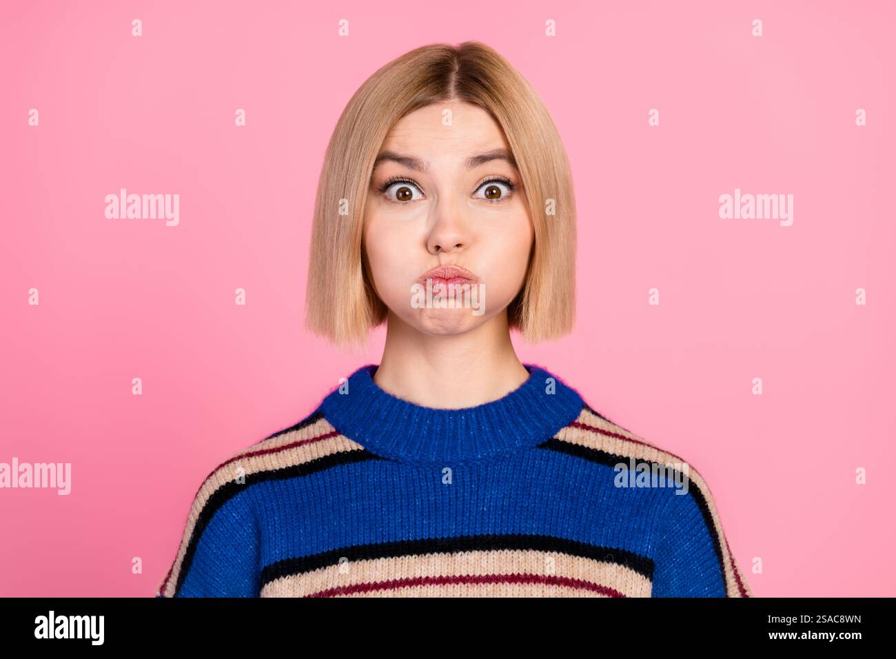 Funny woman puffing her cheeks in a trendy striped sweater against a ...