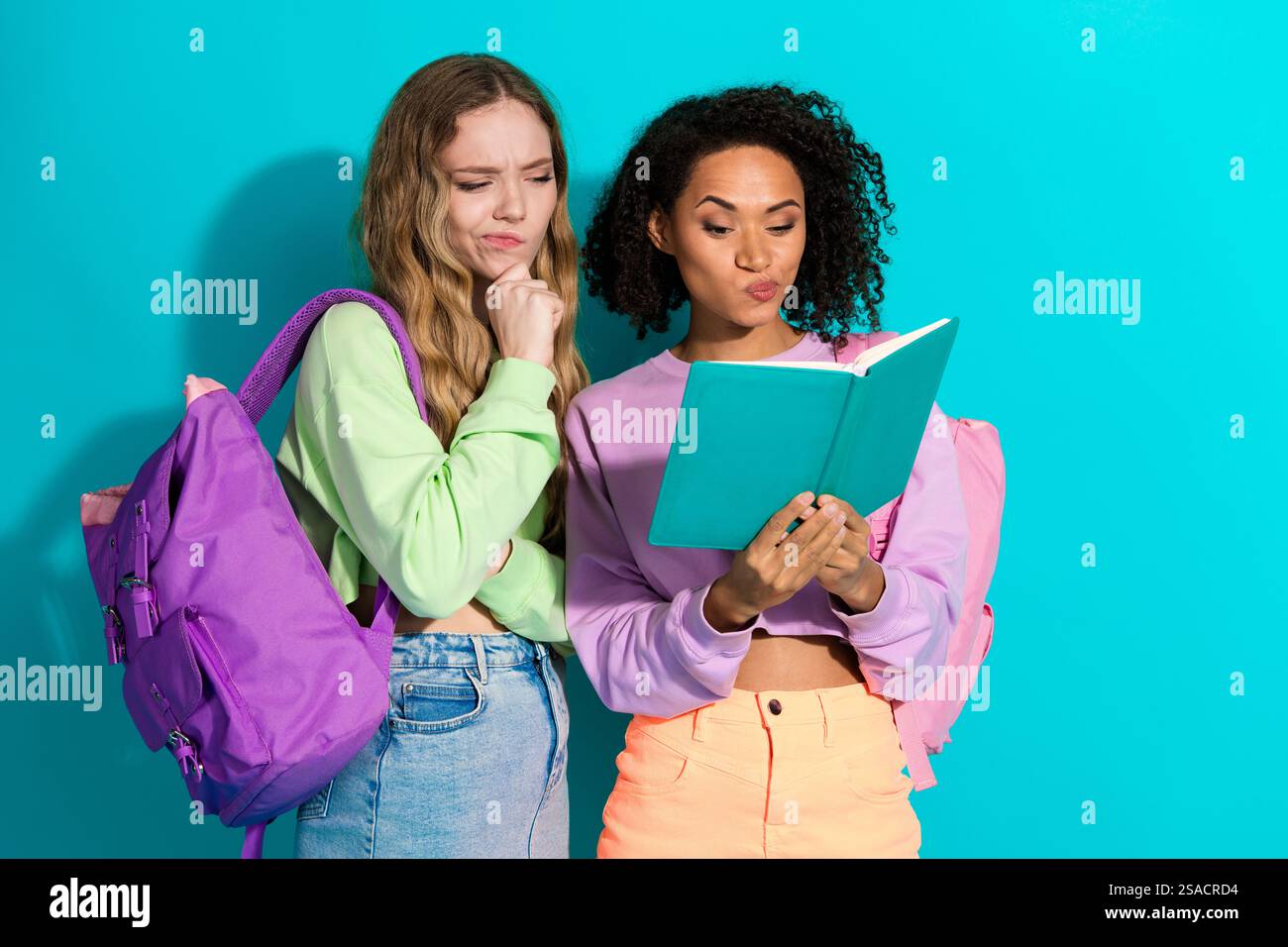Two young female students in colorful clothes reading a book together ...