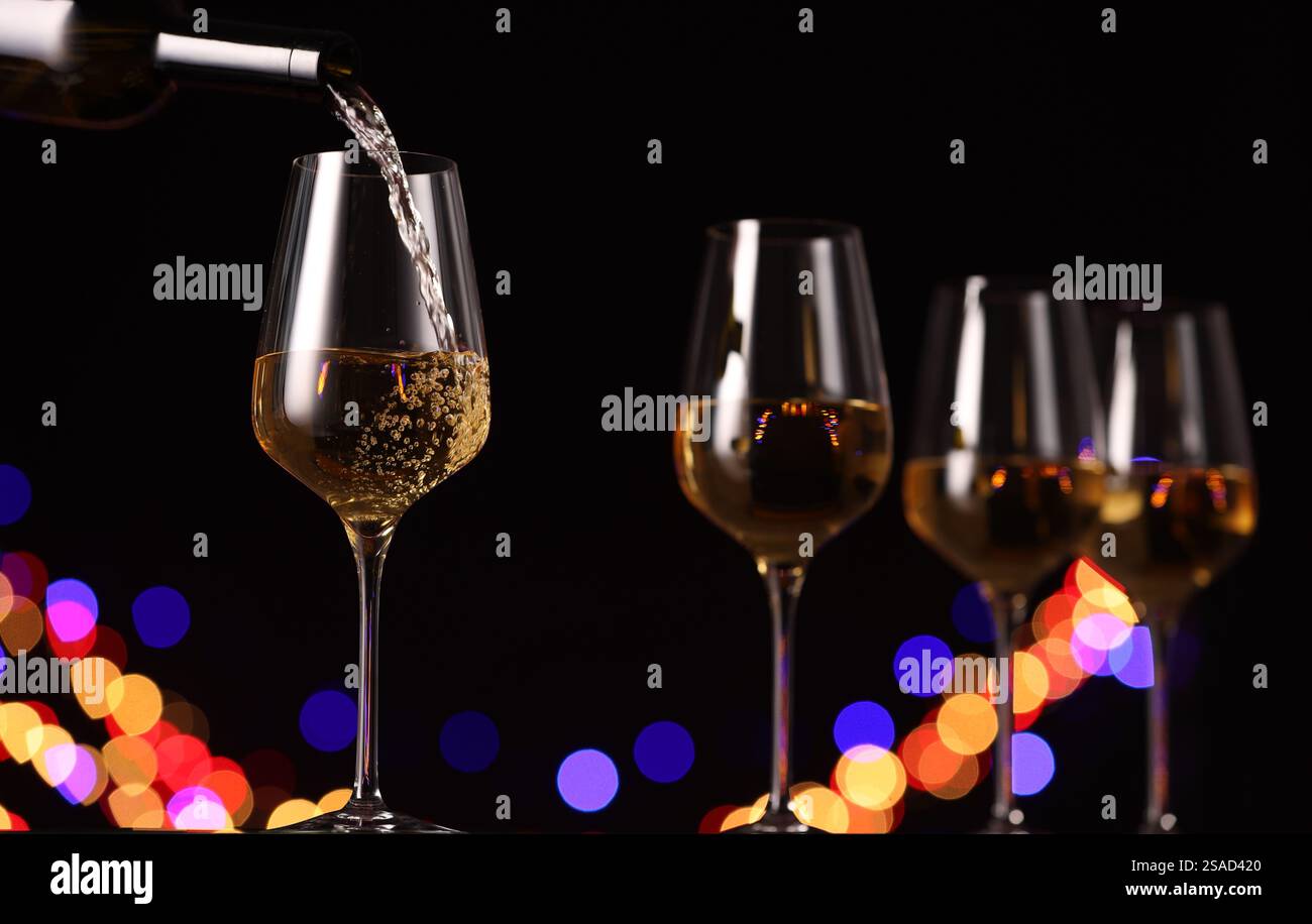 Pouring white wine into glass against black background with blurred ...