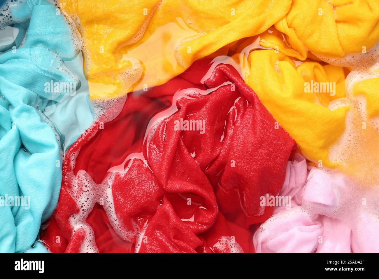 Colorful clothes soaked in water before washing, top view Stock Photo ...
