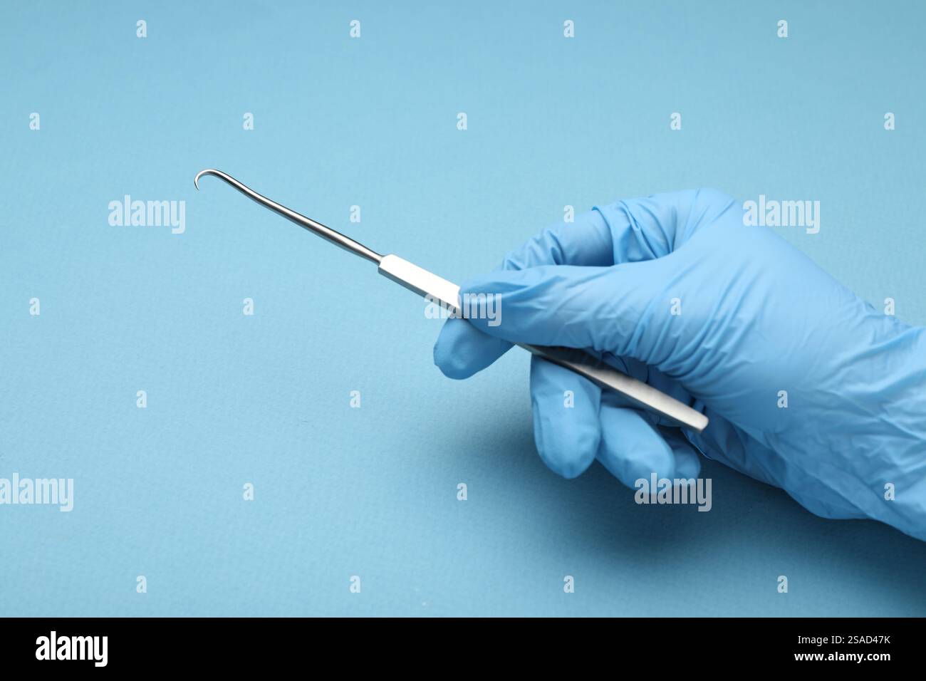Doctor with surgical hook on light blue background, closeup. Space for ...