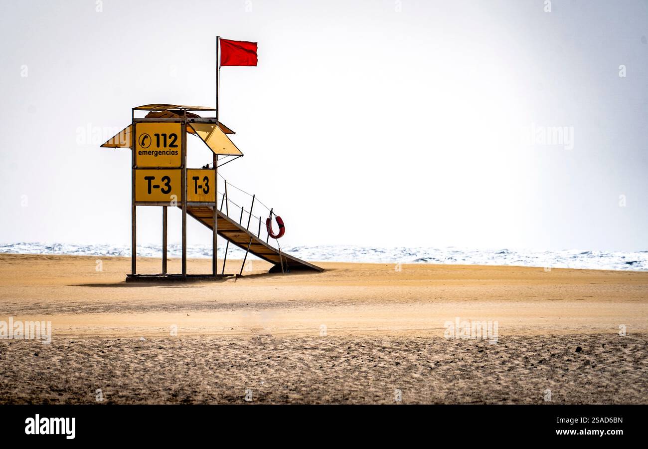 A lifeguard tower on a deserted beach with a red warning flag flying ...