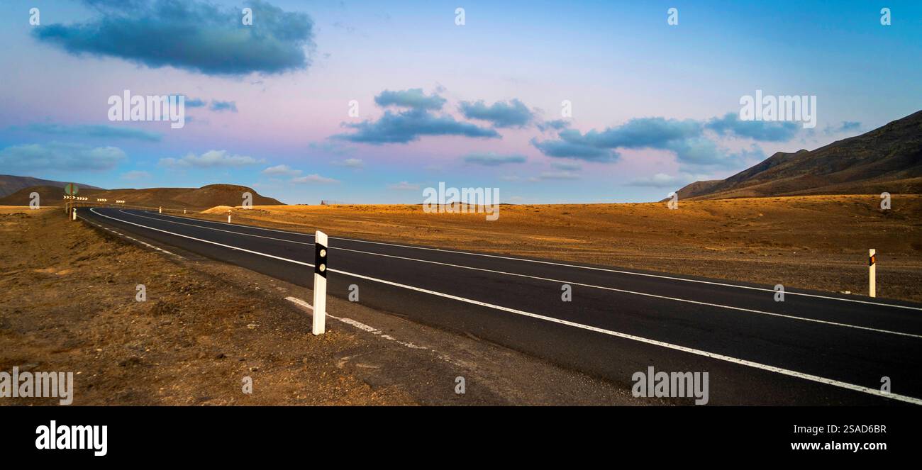 A long, empty road stretches through a barren landscape under a pastel ...