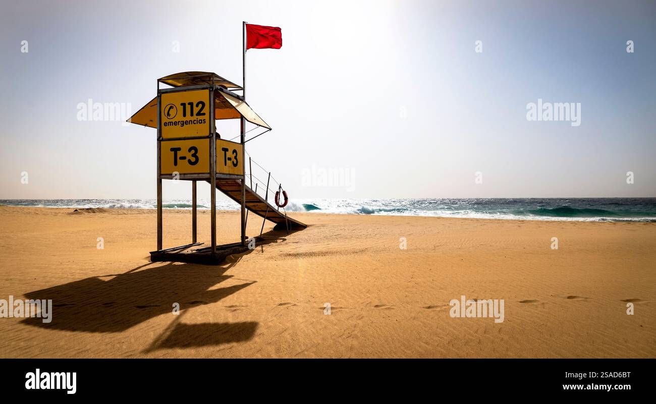 A lifeguard tower on a sandy beach with a red flag flying, indicating ...