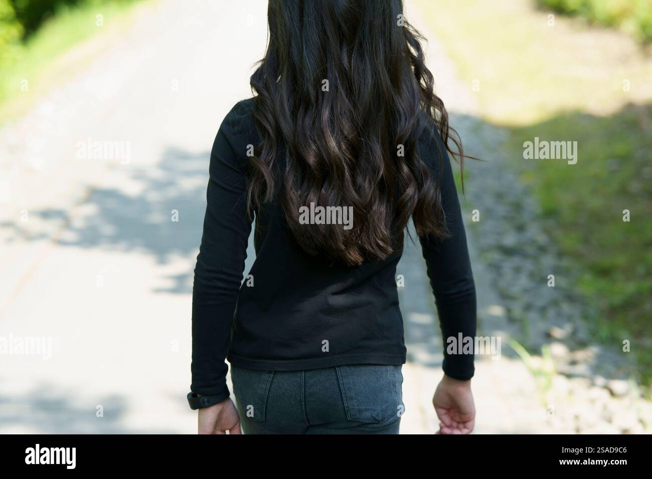 Girl with long dark curly hair walking on a park path in summer. Child ...
