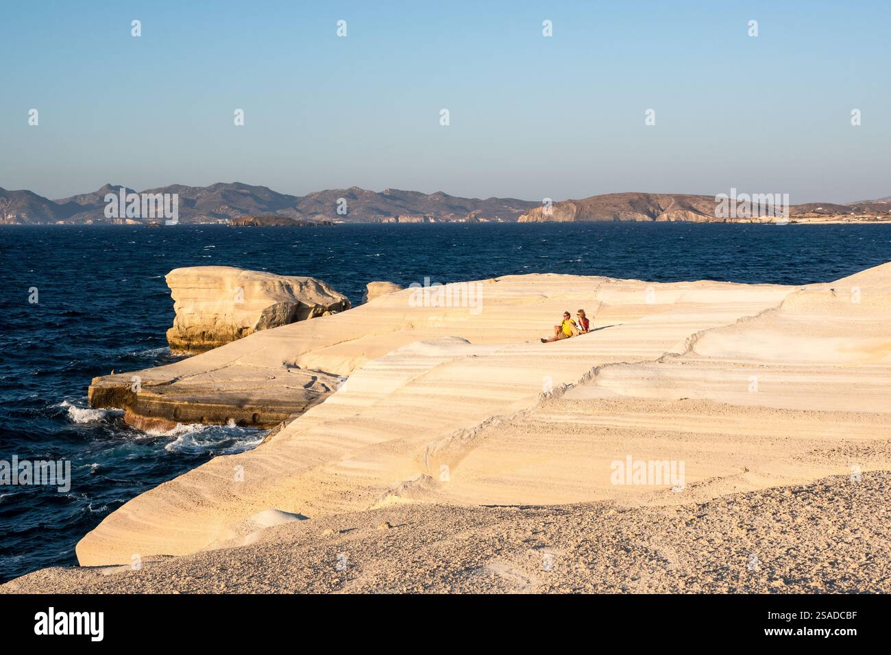 Mature couple of travelers enjoying sunset on rocky shore with ...