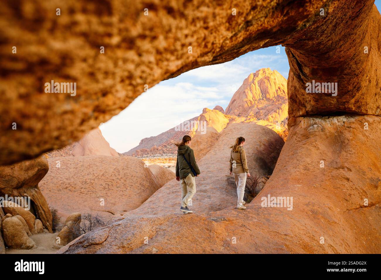Family mother and two kids hiking in Spitzkoppe area with picturesque stone arches and unique ...