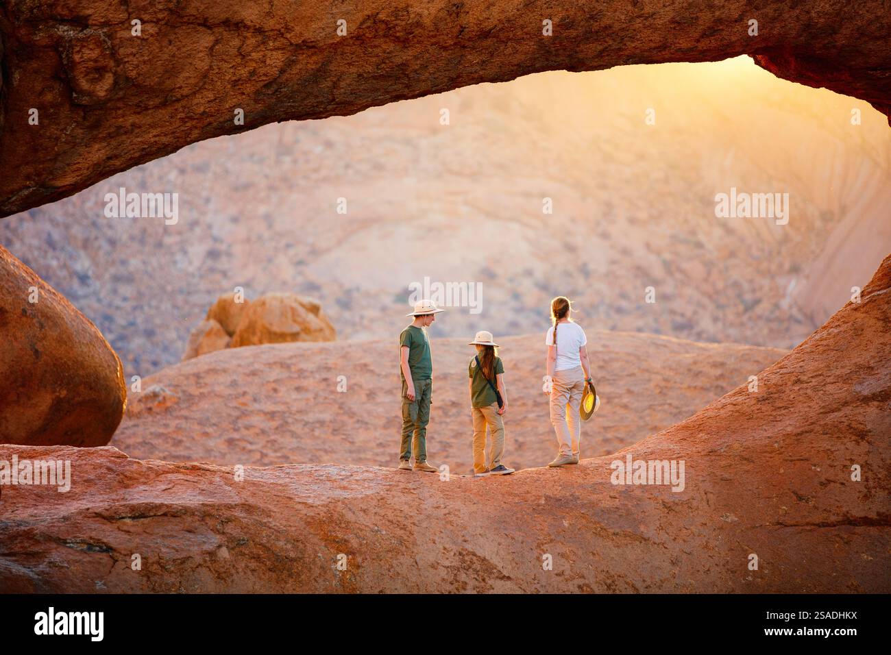 Family mother and two kids hiking in Spitzkoppe area with picturesque stone arches and unique ...