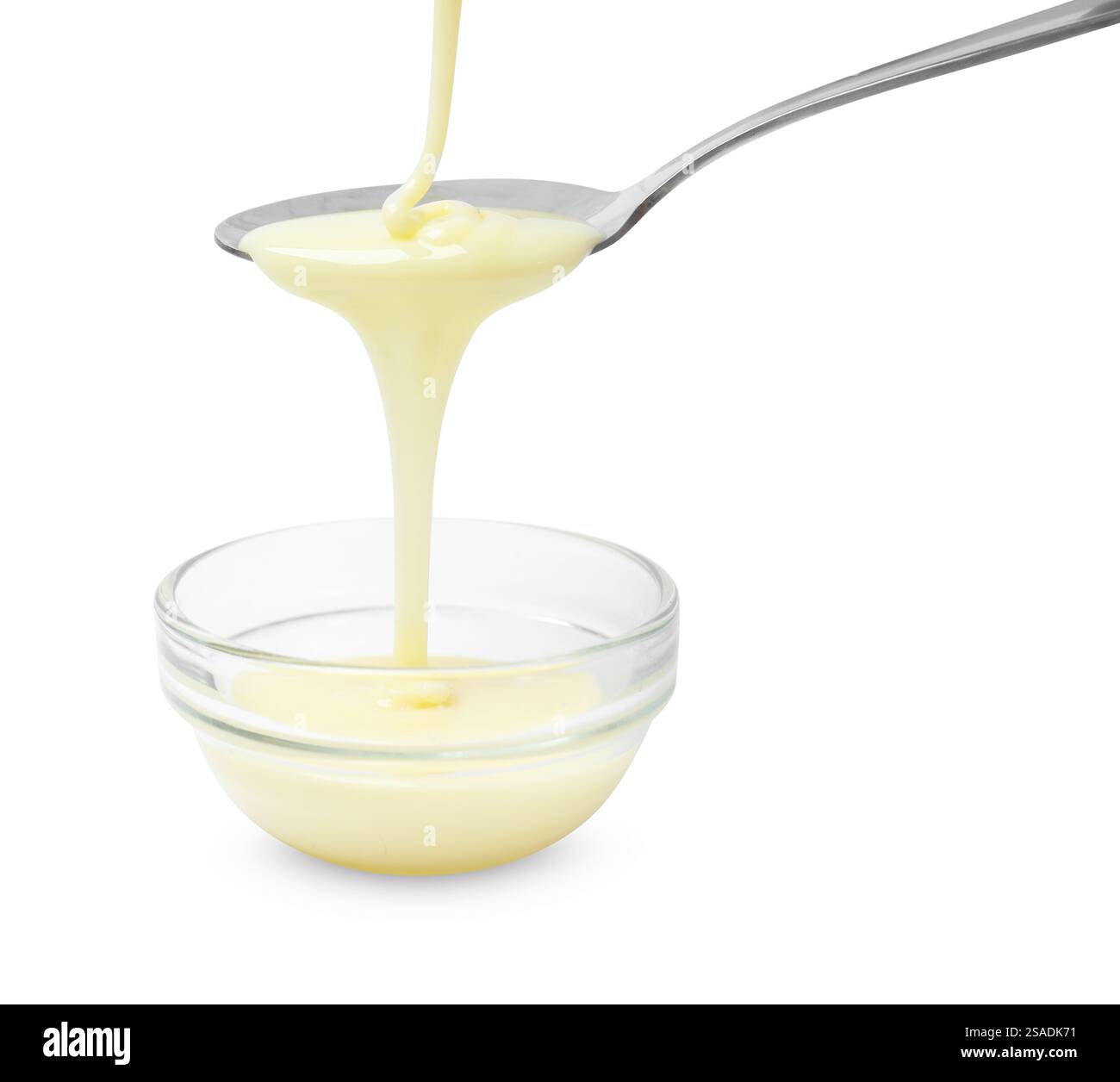 Condensed milk flowing down from spoon into bowl isolated on white ...