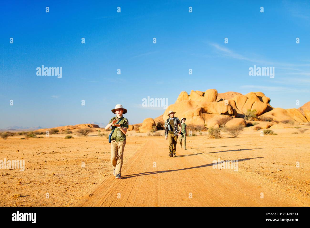 Family father and two kids hiking in Spitzkoppe area with unique rock formations in Damaraland ...